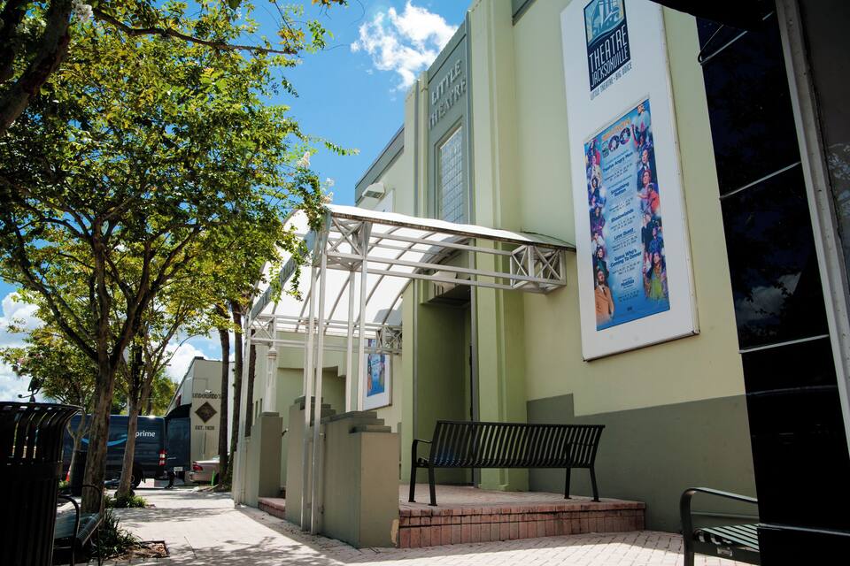 Um edifício de teatro com fachada verde, um banco preto e um cartaz anunciando um espetáculo.