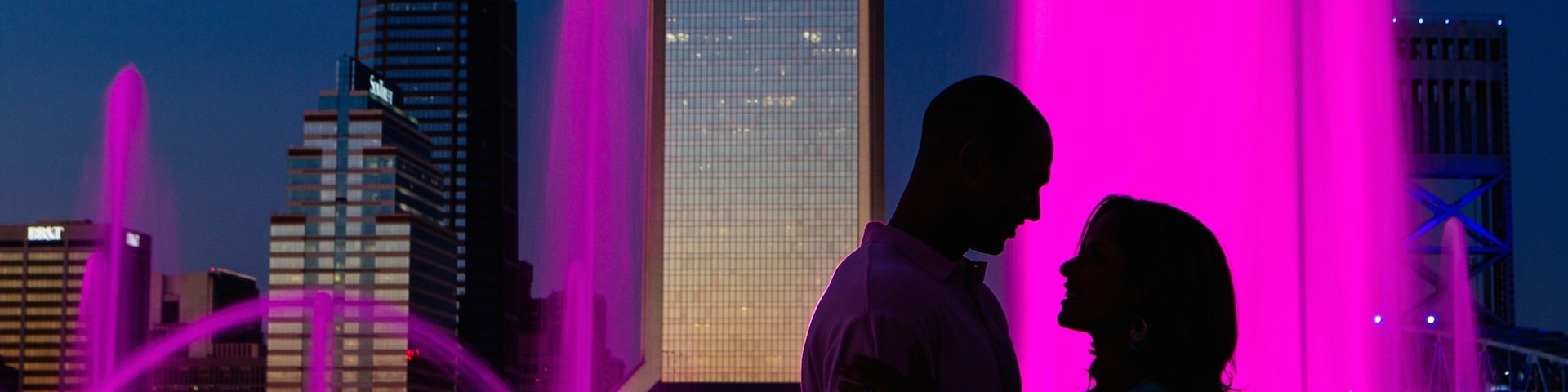 Um casal se abraçando em frente a um horizonte urbano com edifícios iluminados, incluindo um edifício Wells Fargo.