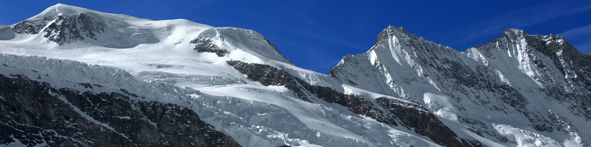 Cordilheira nevada com picos afiados sob um céu azul límpido.