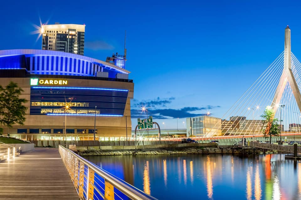 Um edifício moderno com a sinalização 'GARDEN', uma orla marítima e uma ponte atirantada.