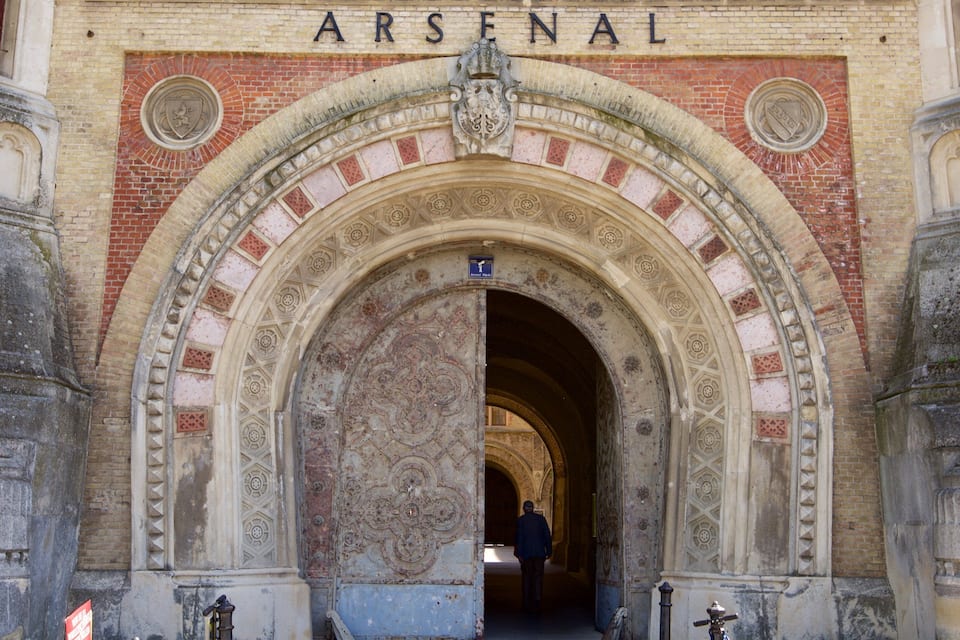 Arcada ornamentada com a palavra "ARSENAL" acima, dando acesso a um edifício.