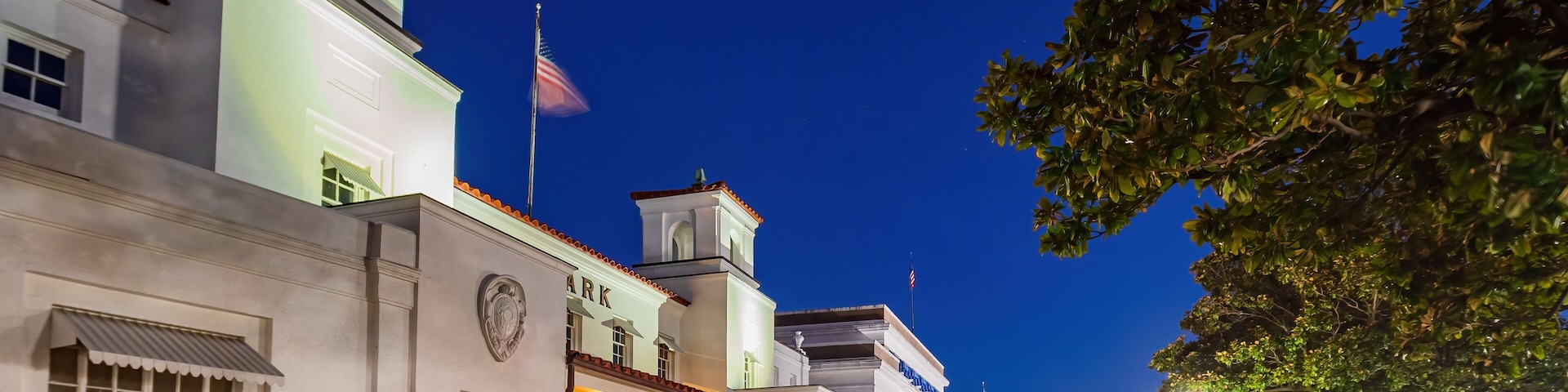 Um edifício histórico com uma torre do relógio, uma bandeira e um caminho bem iluminado.