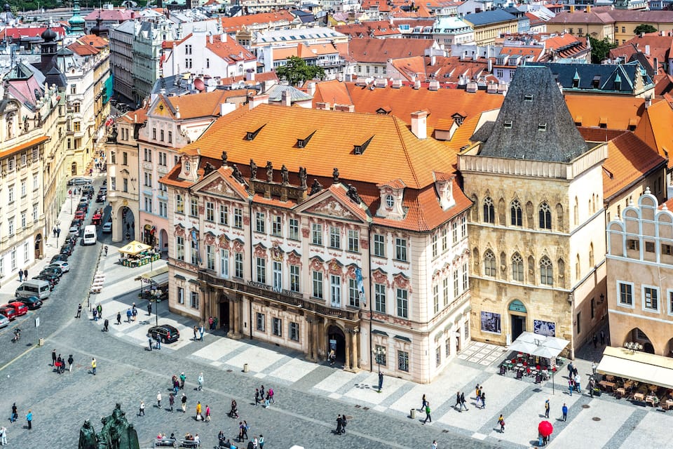 Uma praça histórica com um edifício imponente, com telhado de telhas vermelhas e arquitetura elaborada.