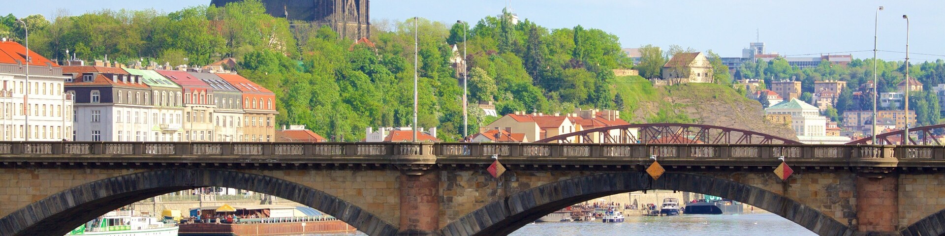 Uma ponte de pedra sobre um rio, com um barco em primeiro plano e uma catedral ao fundo.