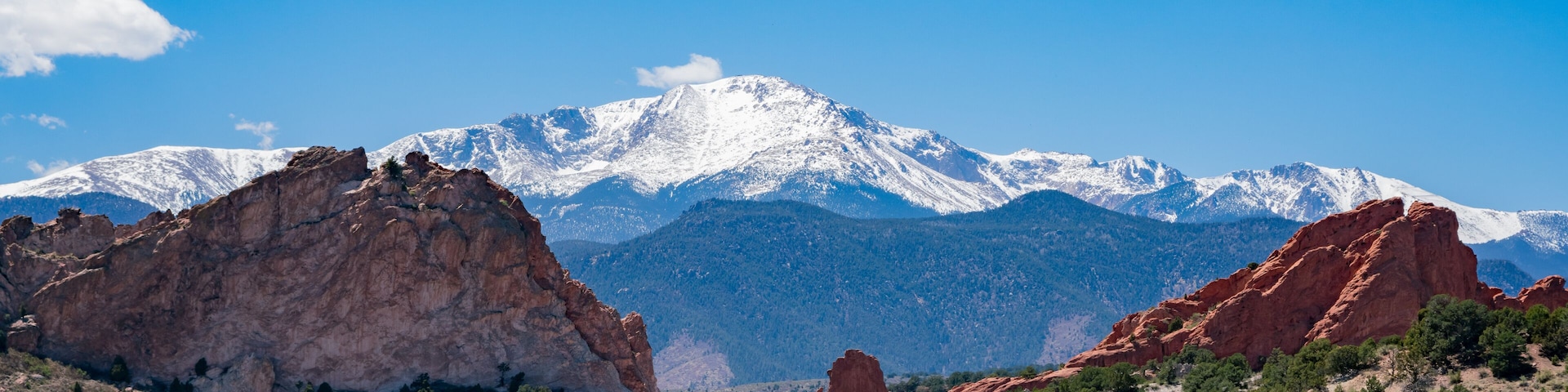 Cordilheira com picos nevados, formações rochosas avermelhadas e céu azul límpido.