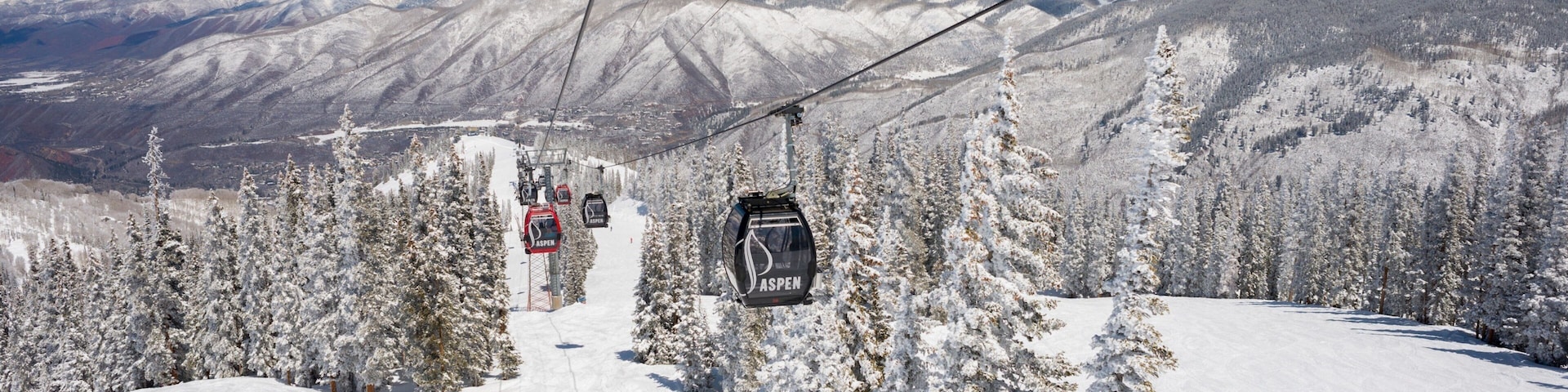 Um teleférico em uma paisagem montanhosa coberta de neve, com árvores carregadas de neve e montanhas ao longe.
