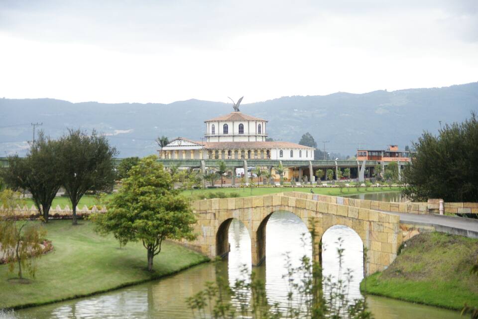 Uma ponte de pedra sobre um rio calmo, um edifício grande com cúpula e um cenário montanhoso ao fundo.