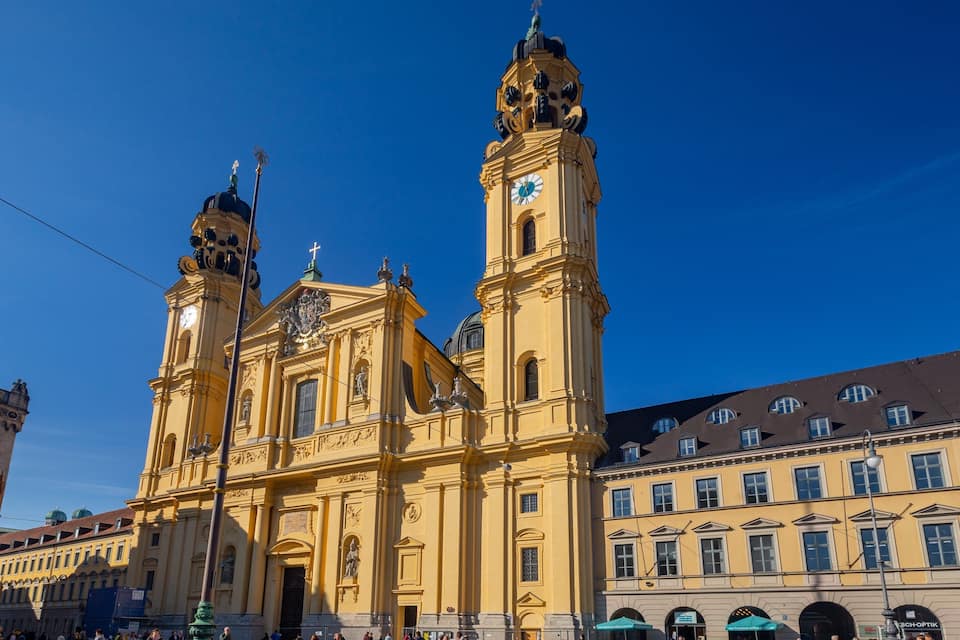 Uma igreja amarela histórica com duas torres e um grande relógio.