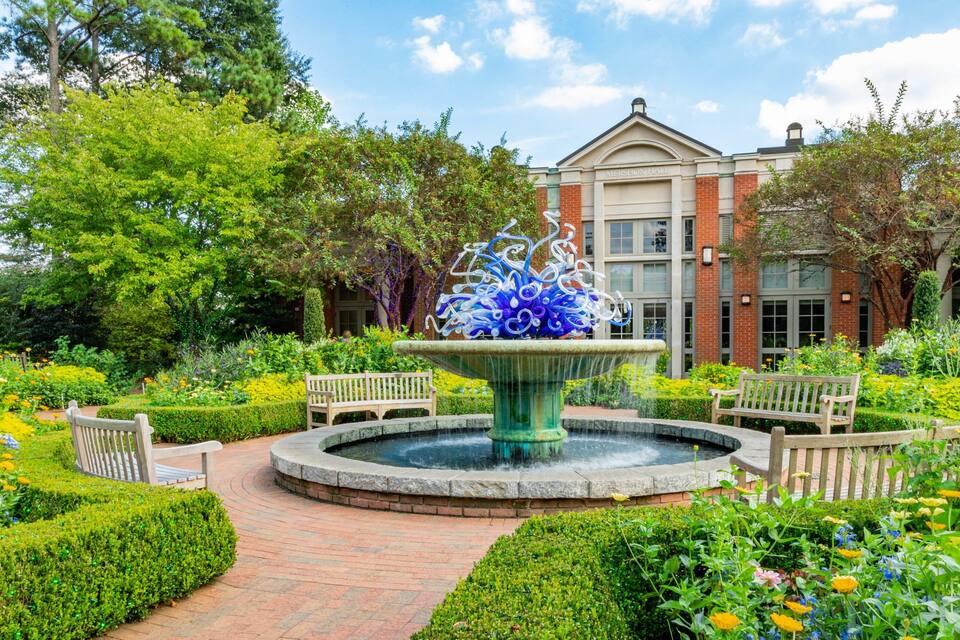 Um jardim com uma fonte, bancos e um edifício identificado como 'Fashion Hall'.