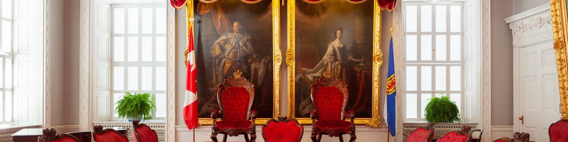 Sala de reuniões formal com uma longa mesa de madeira, cadeiras estofadas em vermelho e um quadro grande com a imagem de duas figuras na parede.