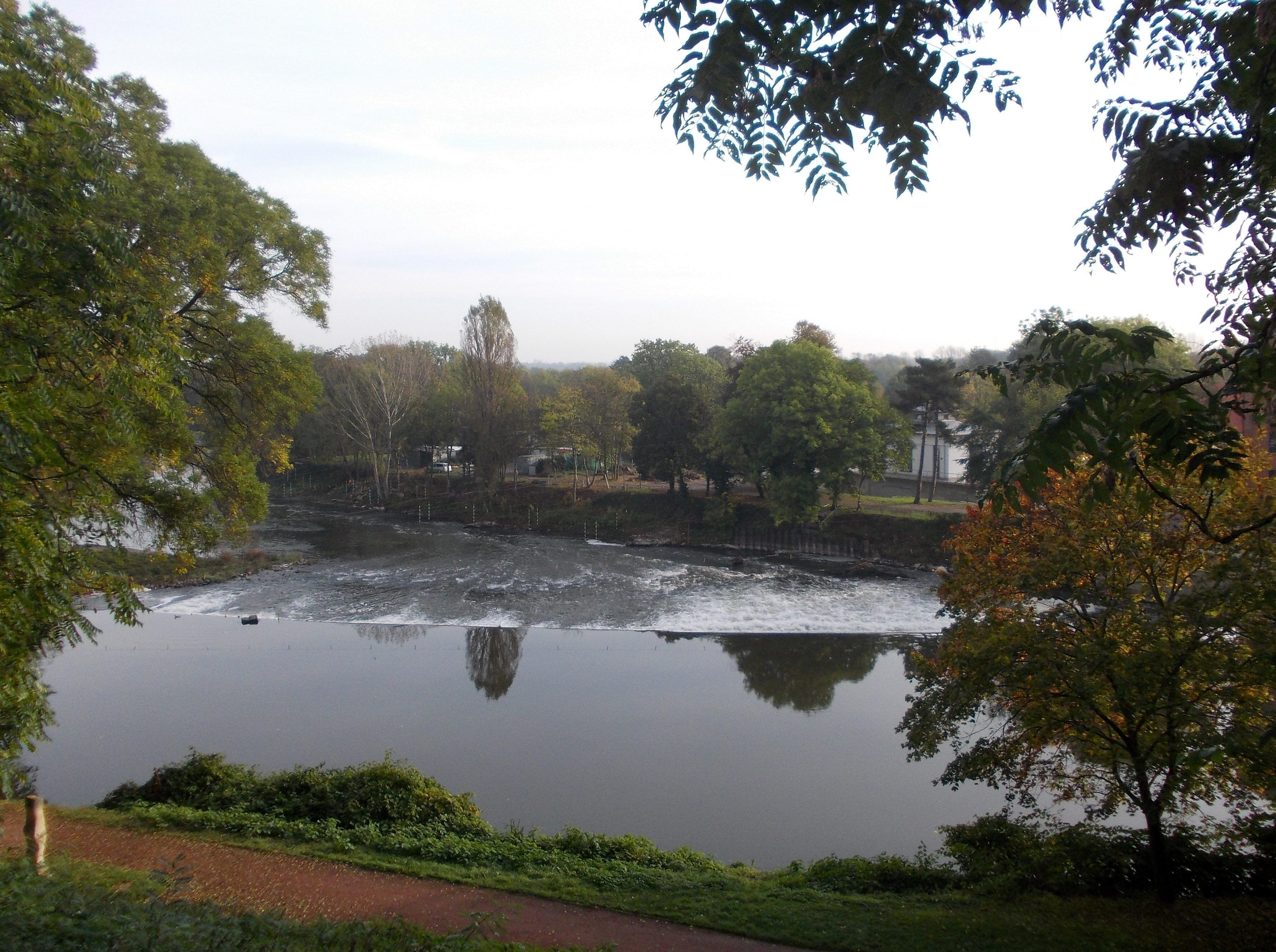 Um lago tranquilo rodeado de árvores e um edifício ao longe.