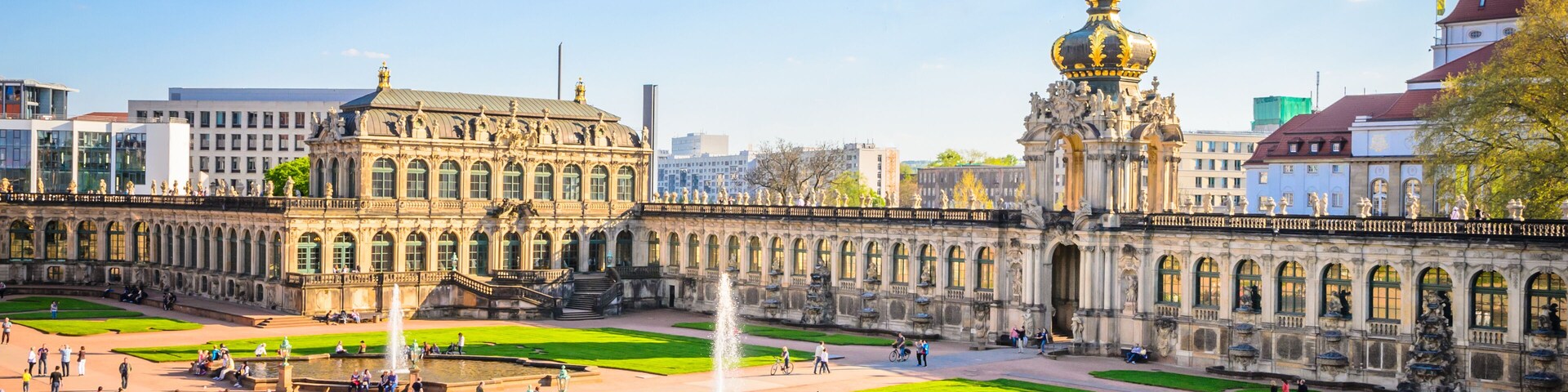 Um palácio imponente com uma fonte, jardins bem cuidados e um céu azul límpido.
