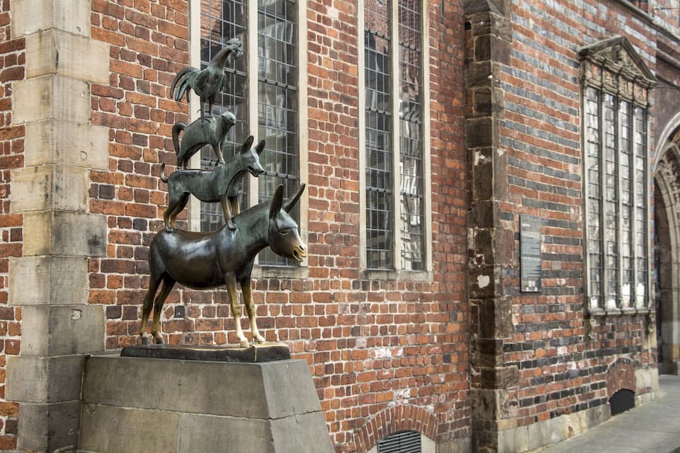 Uma estátua de três animais sobre um pedestal, em frente a um edifício de tijolos com grandes janelas.