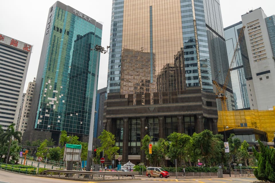 Paisagem urbana com edifícios modernos e altos, incluindo um edifício com fachada em forma de grade e outro com exterior de padrão único.