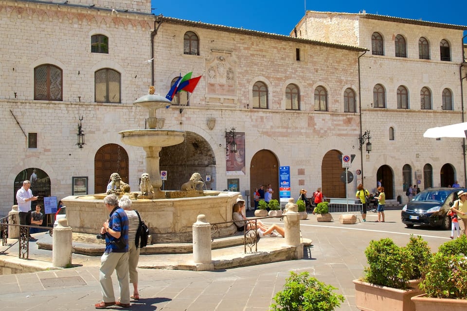 Uma praça histórica com uma fonte, edifícios de pedra e uma bandeira.