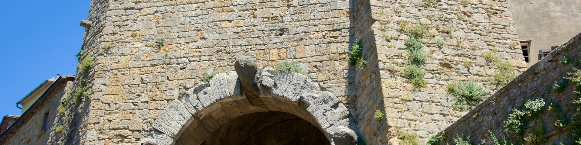 Um arco de pedra em um edifício antigo, com um céu azul claro ao fundo.