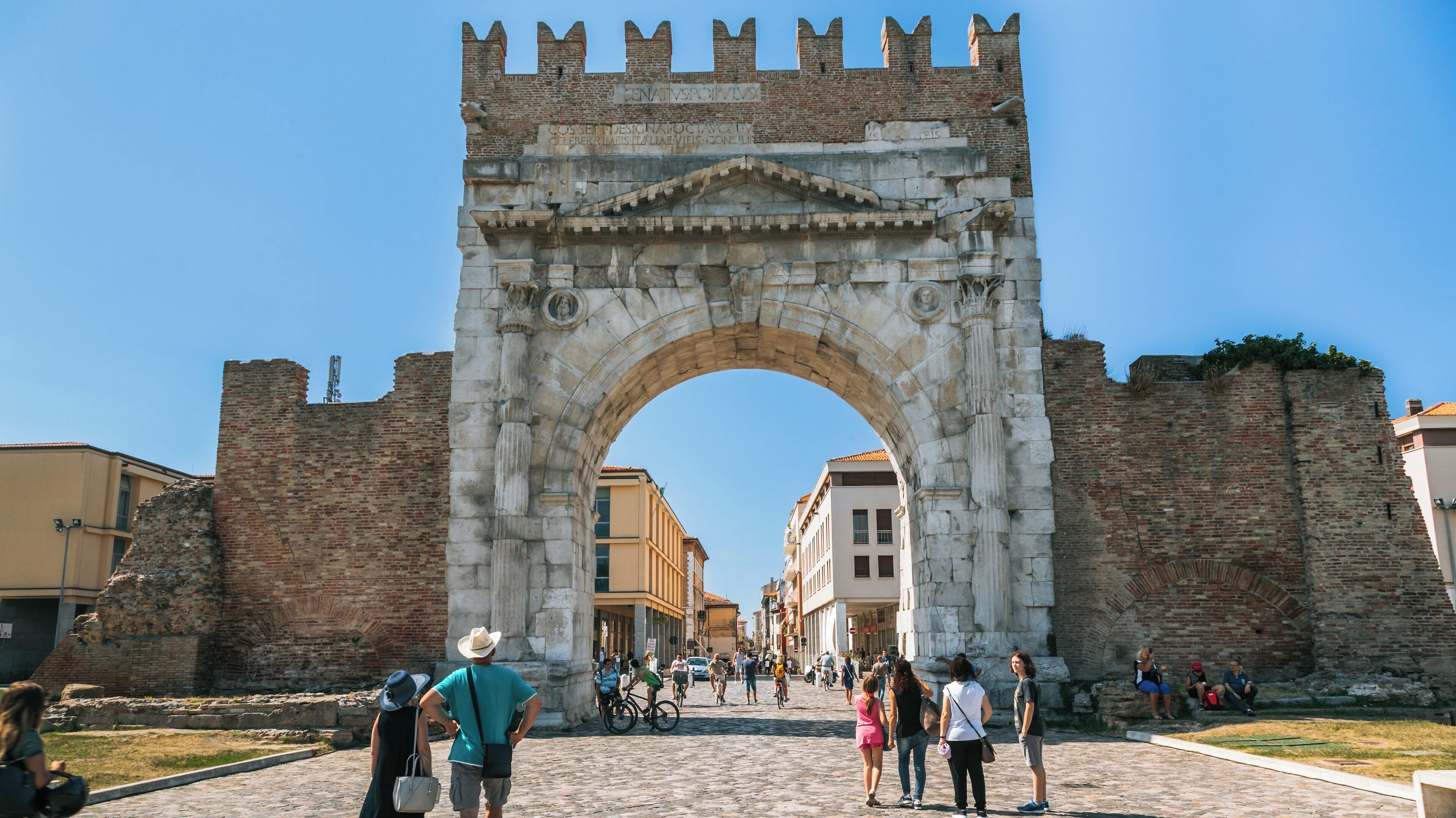 Historical significance of the Arch of Augustus in Rimini, Emilia-Romagna, Italy, surrounded by visitors on a sunny day