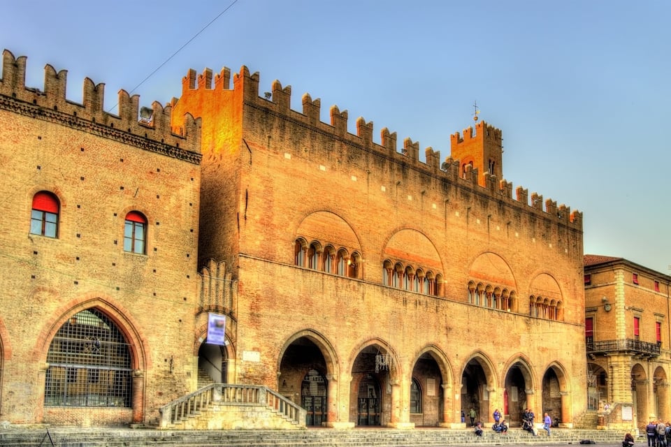 Um edifício histórico de tijolos com janelas em arco e uma muralha fortificada.