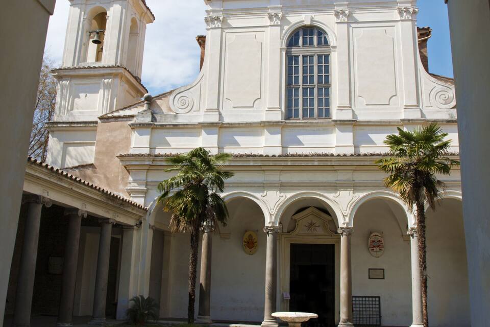 Uma igreja branca com torre sineira e palmeiras no pátio.