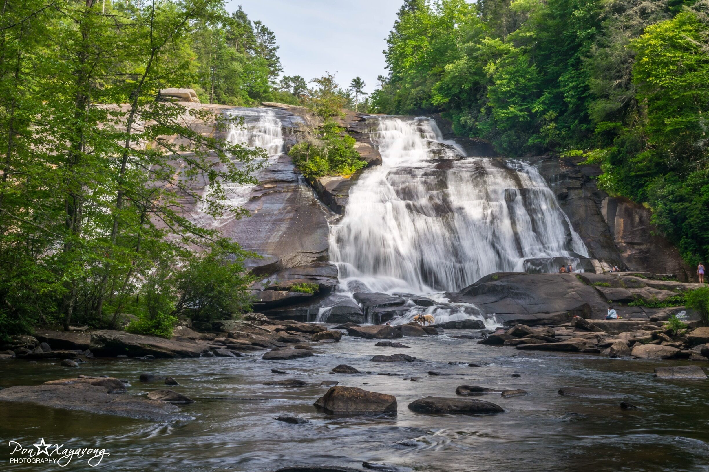 Uma cascata descendo sobre pedras, cercada por vegetação exuberante.