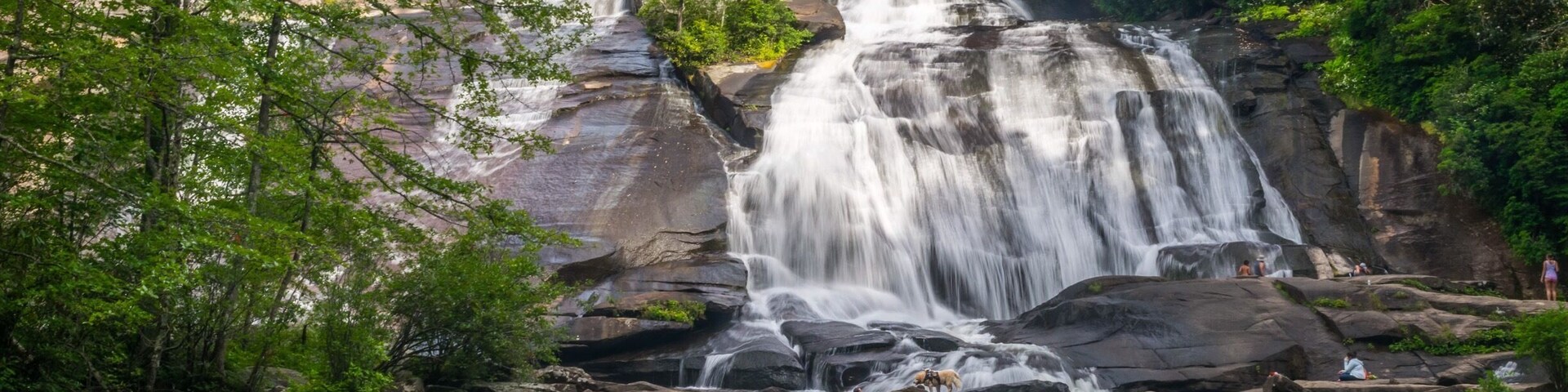 Uma cascata descendo sobre pedras, cercada por vegetação exuberante.