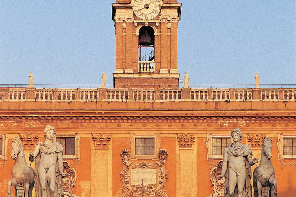 Um edifício histórico com uma torre do relógio, estátuas e arquitetura ornamentada.