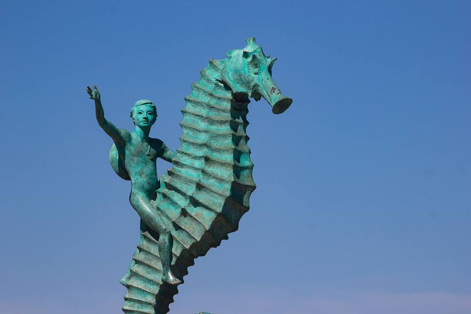 Estátua de um homem montado em um cavalo-marinho, com um céu limpo ao fundo.