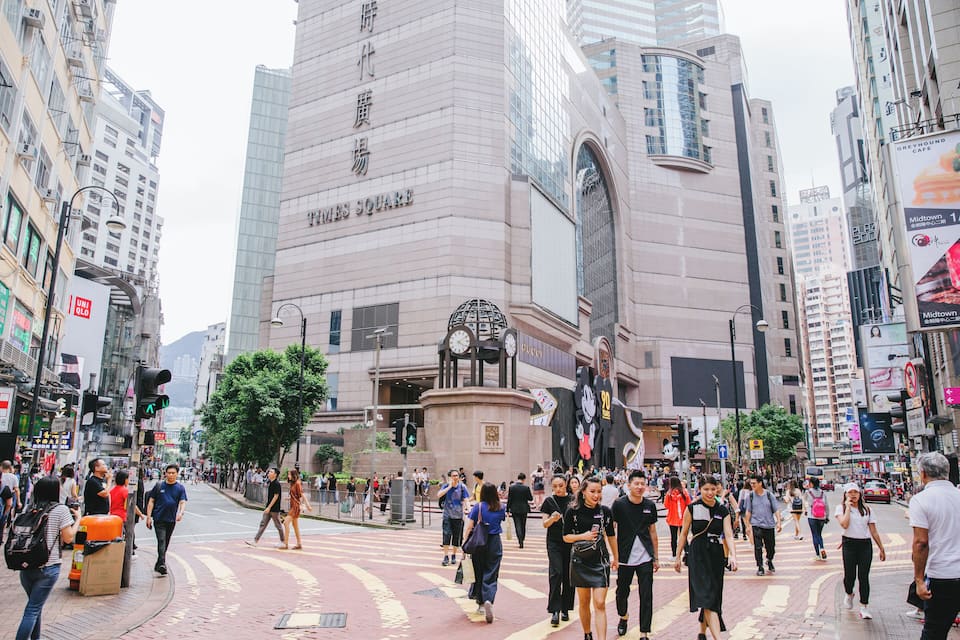 Um movimentado cruzamento urbano com pedestres atravessando, cercado por edifícios altos e diversos letreiros comerciais.