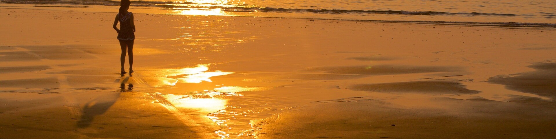 Uma praia ao pôr do sol com uma pessoa em pé na areia.