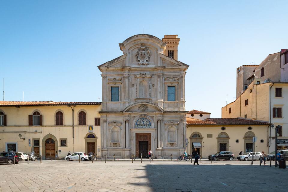 Um edifício histórico com entrada central, janelas em arco e telhado em telhas.