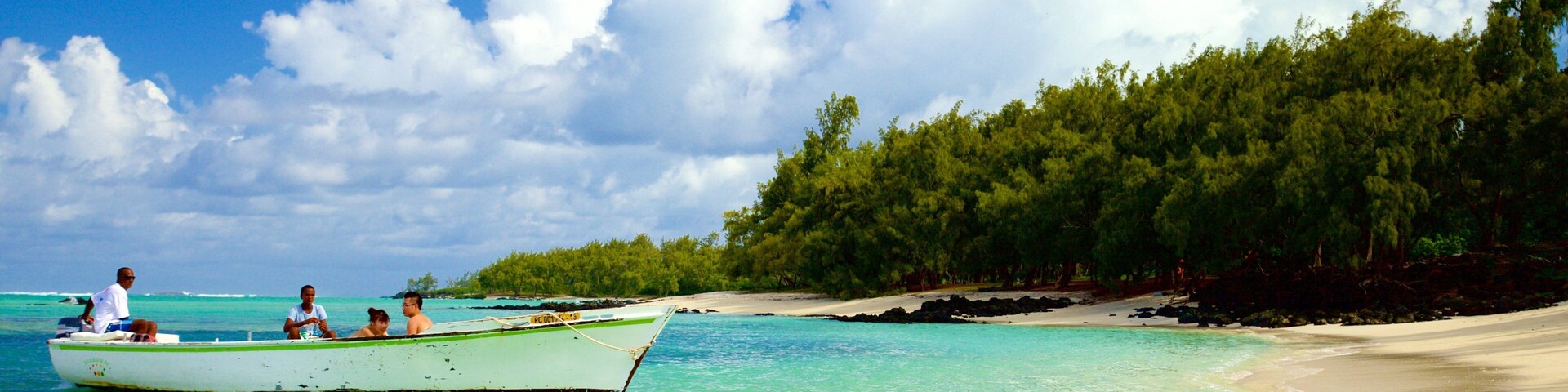 Um barco em águas azul-turquesa, uma praia de areia e uma área arborizada.