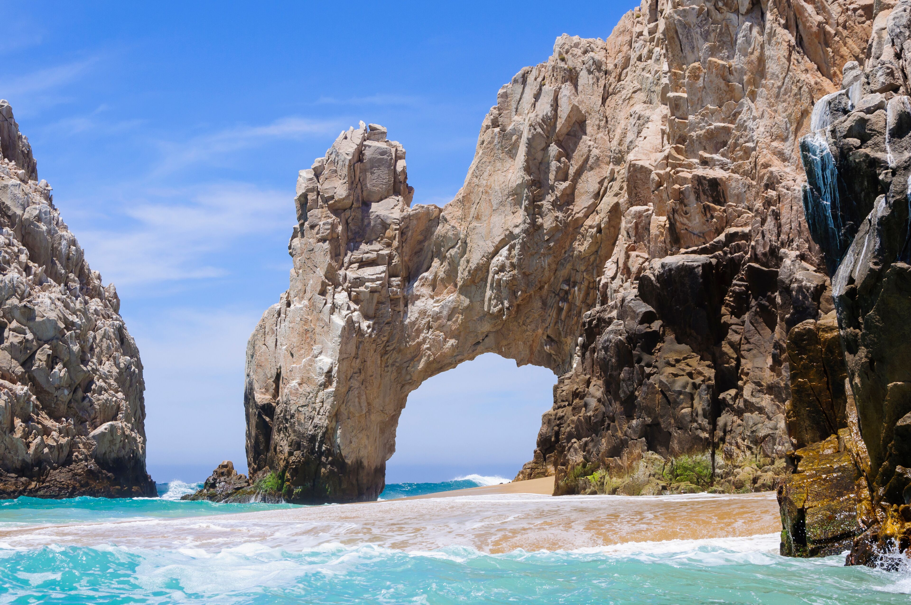 Formação rochosa em arco costeiro com uma praia ao primeiro plano.