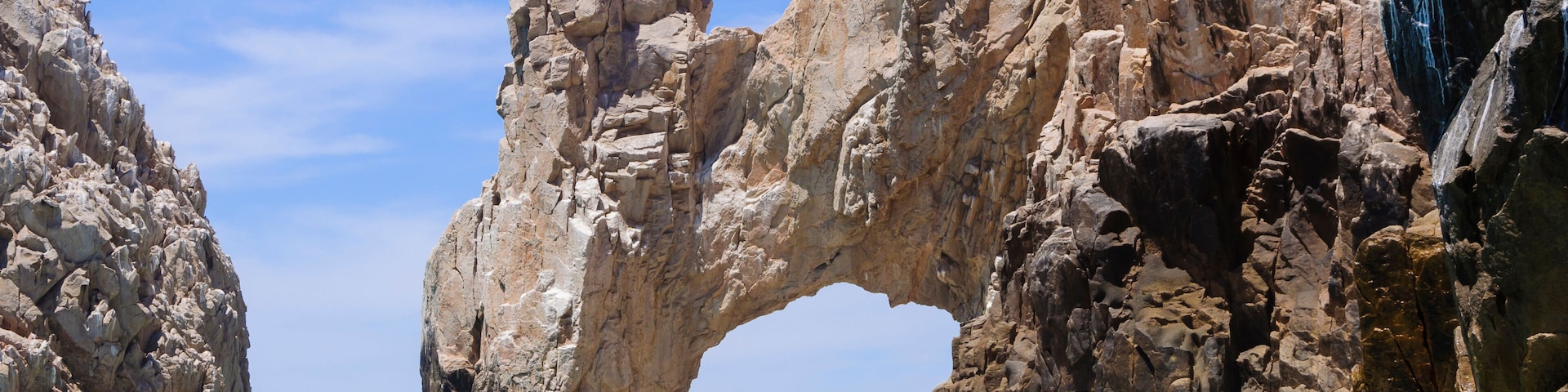 Formação rochosa em arco costeiro com uma praia ao primeiro plano.