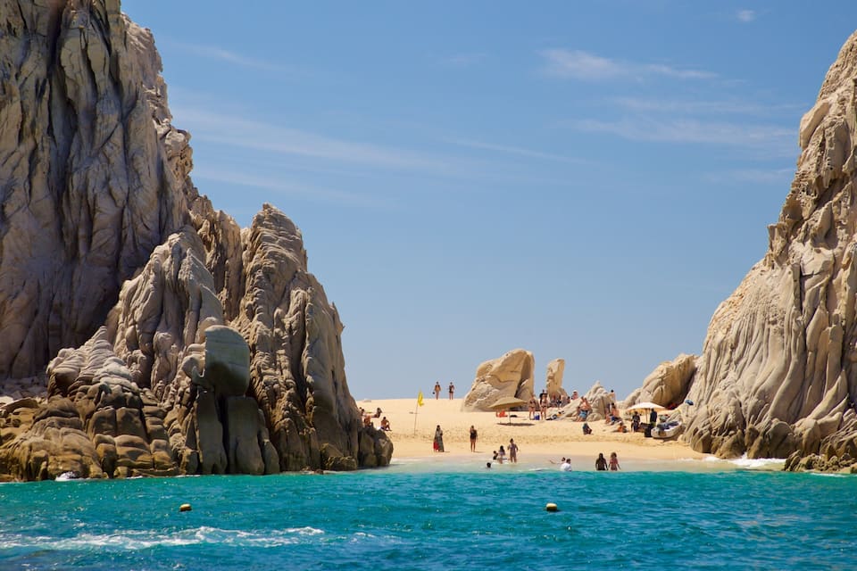 Costa rochosa com águas turquesa cristalinas e uma praia de areia.