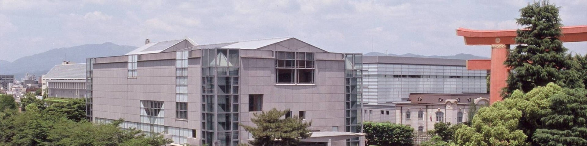 Um edifício moderno com grandes janelas e um grande portão torii em primeiro plano.