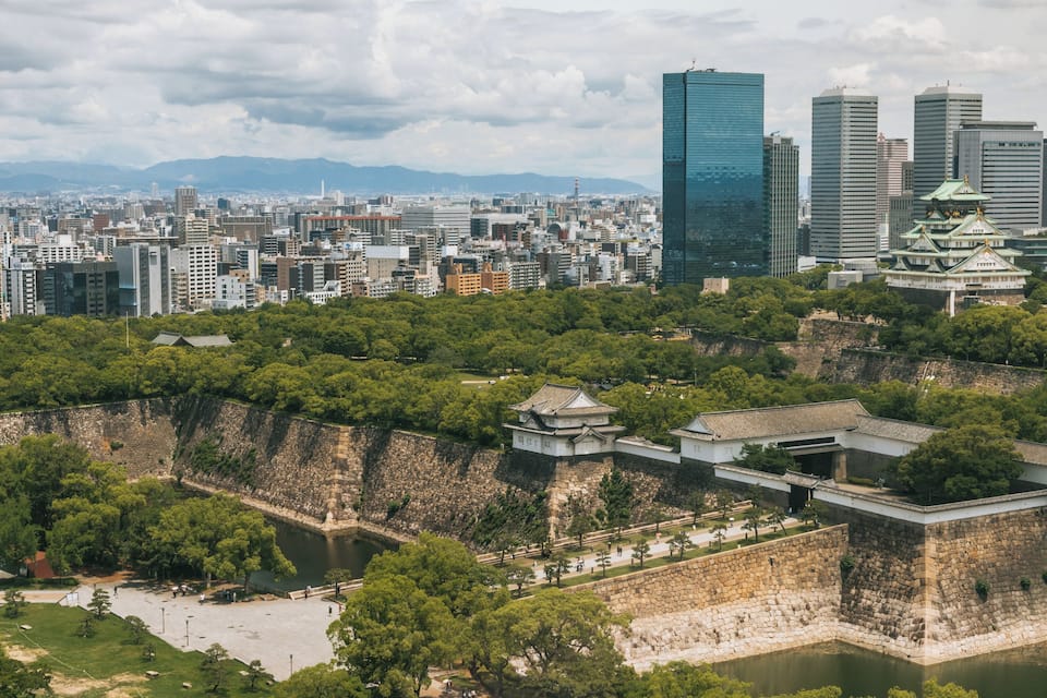 Paisagem urbana com arranha-céus modernos e ruínas de um castelo japonês tradicional.