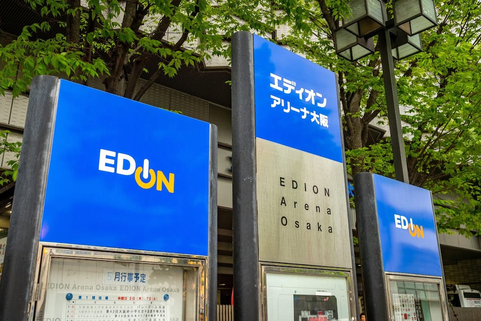 Três placas EDUN em frente a um edifício com árvores e uma estrutura metálica.