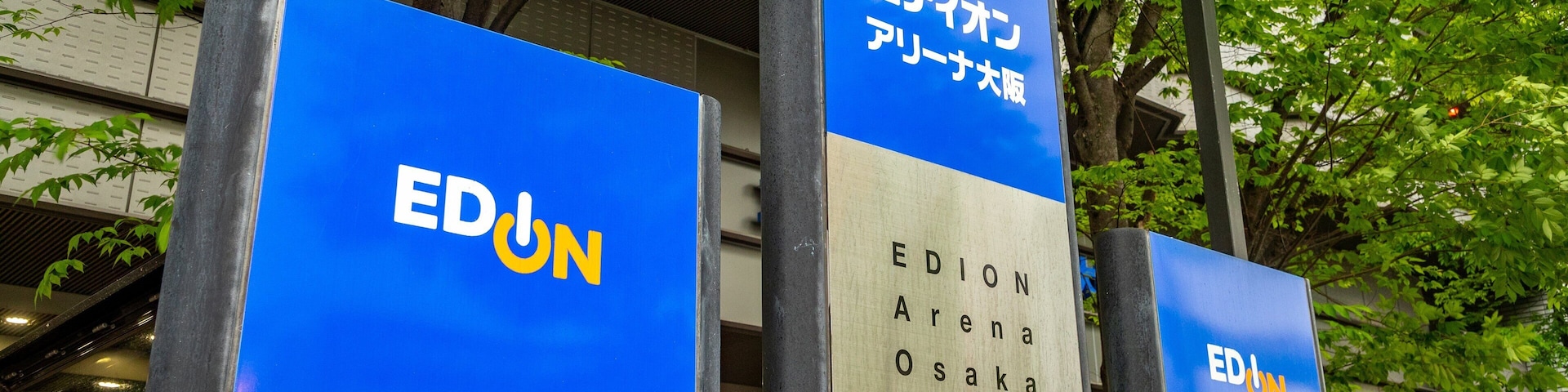 Três placas EDUN em frente a um edifício com árvores e uma estrutura metálica.