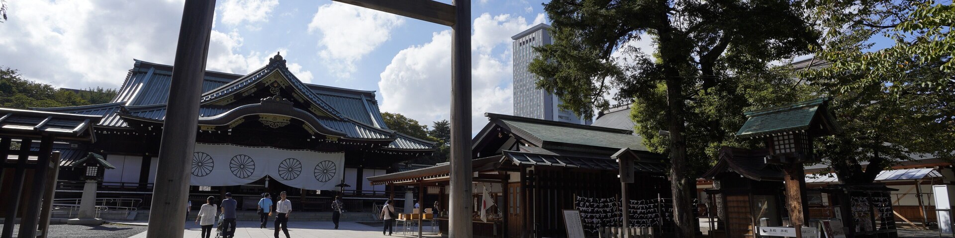 Um templo japonês tradicional com um grande portão torii, rodeado por árvores e um céu limpo.