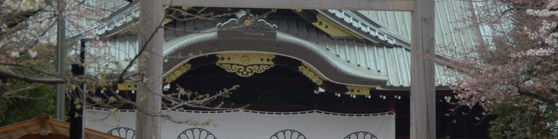 Um edifício japonês tradicional com telhado curvo e padrões decorativos, cercado por flores de cerejeira.