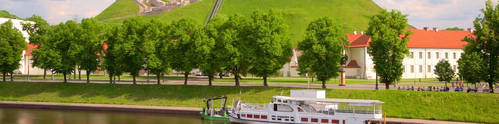 Um rio com um barco, um castelo numa colina e um edifício com telhado vermelho.