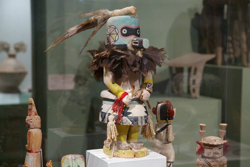 Coleção de artefatos indígenas, incluindo uma figura com cocar emplumado e uma tigela decorada.
