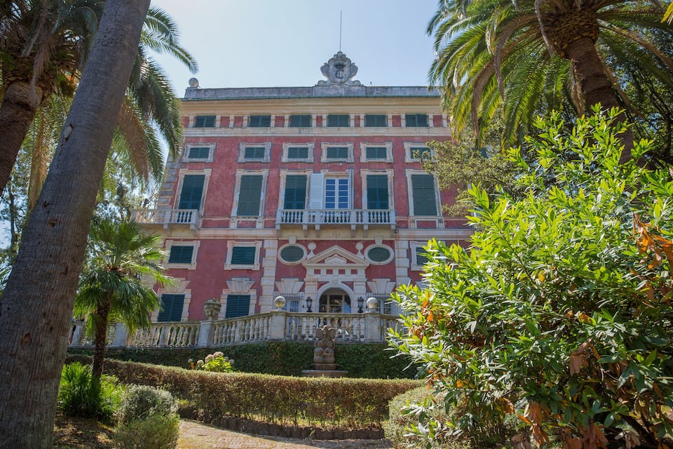 Um edifício grande e histórico com fachada vermelha, persianas verdes e uma varanda central.