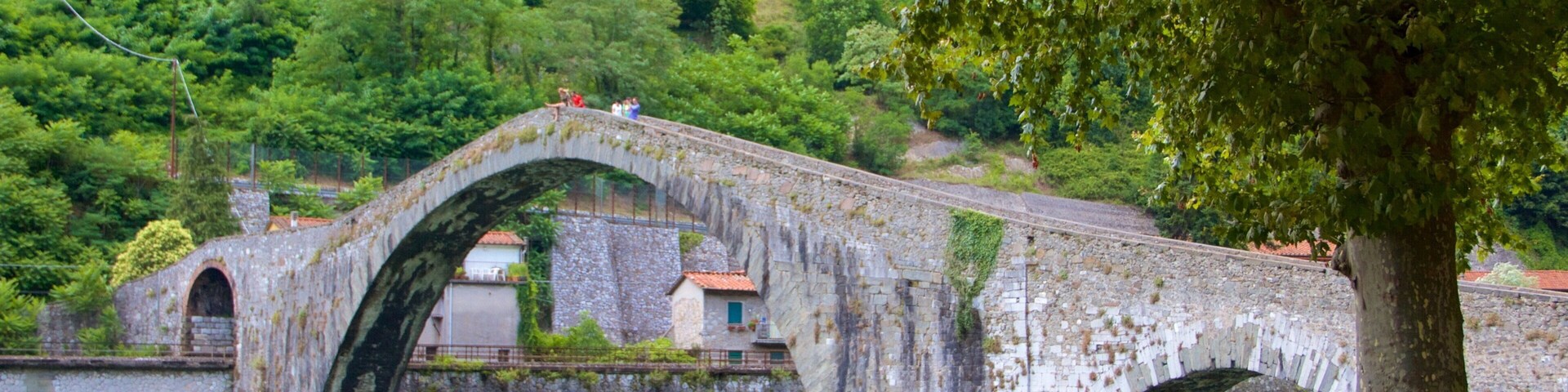 Uma ponte de pedra sobre um rio, cercada por vegetação exuberante e colinas.