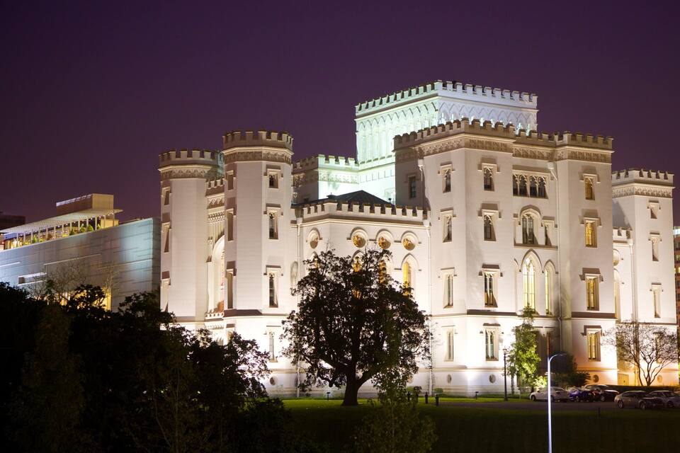 Um grande edifício iluminado, semelhante a um castelo, à noite, com várias torres e janelas em arco.
