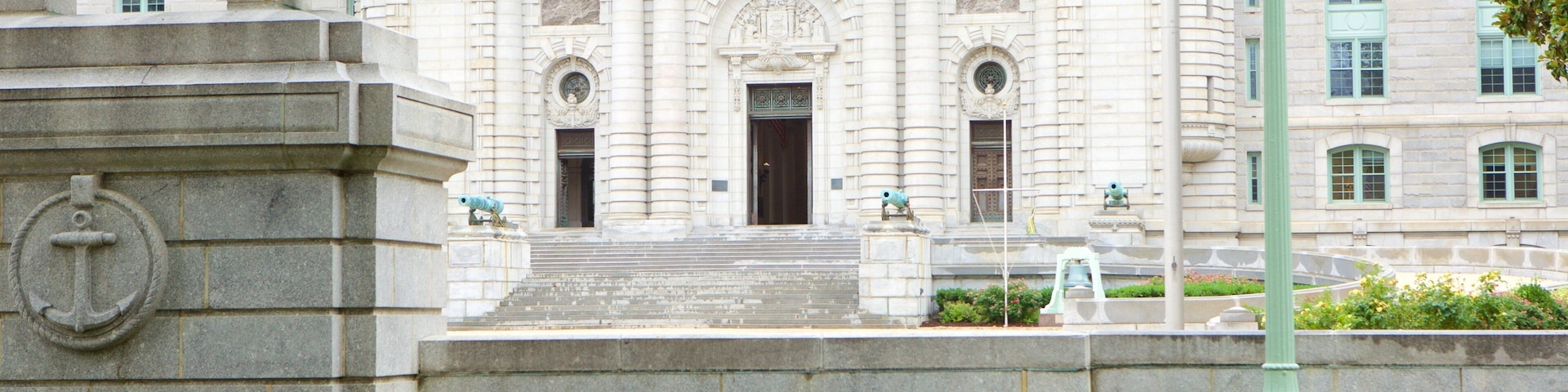 Um edifício grande com arquitetura ornamentada, um canhão e uma placa com a inscrição 'Bancroft Hall'.