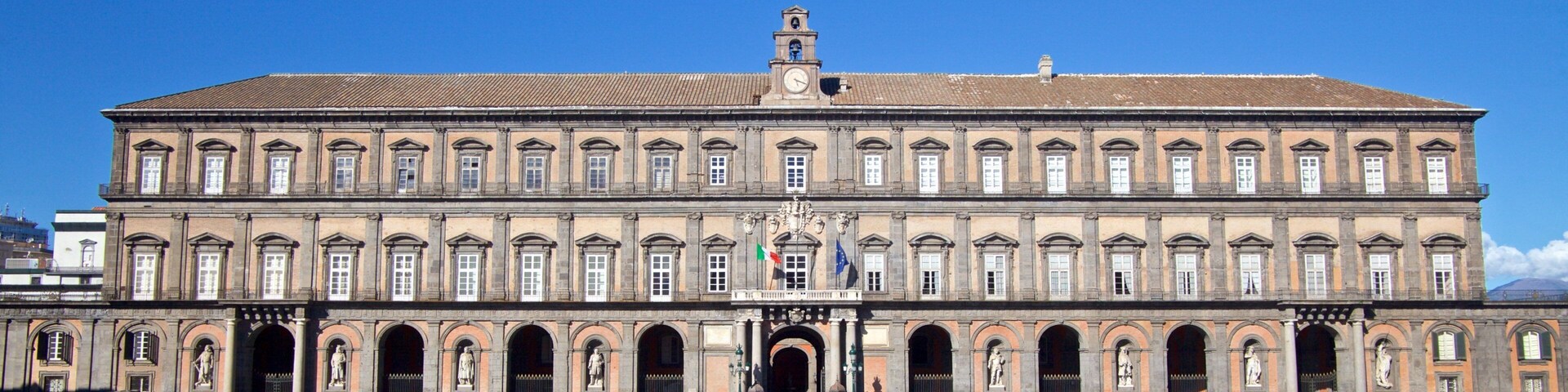 Um grande edifício histórico com uma torre do relógio e várias arcadas.