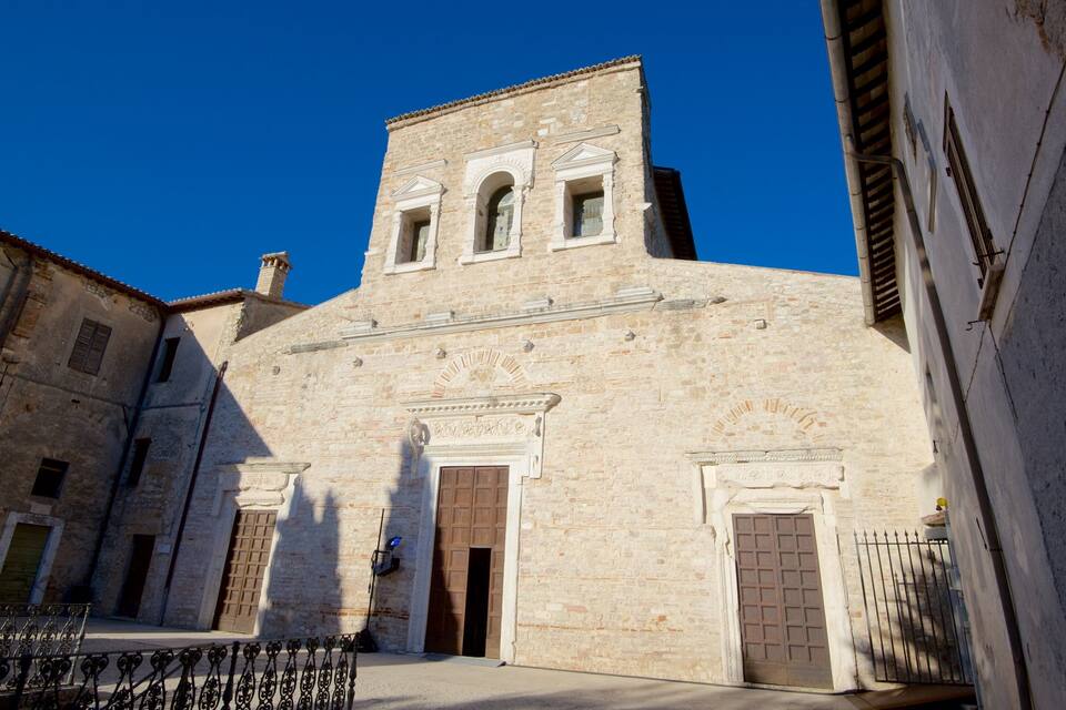 Um edifício histórico de pedra com torre sineira, janelas em arco e um pátio.