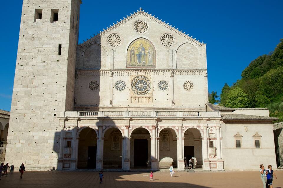 Uma igreja histórica com uma alta torre de sino, fachada ornamentada e uma grande rosácea central.