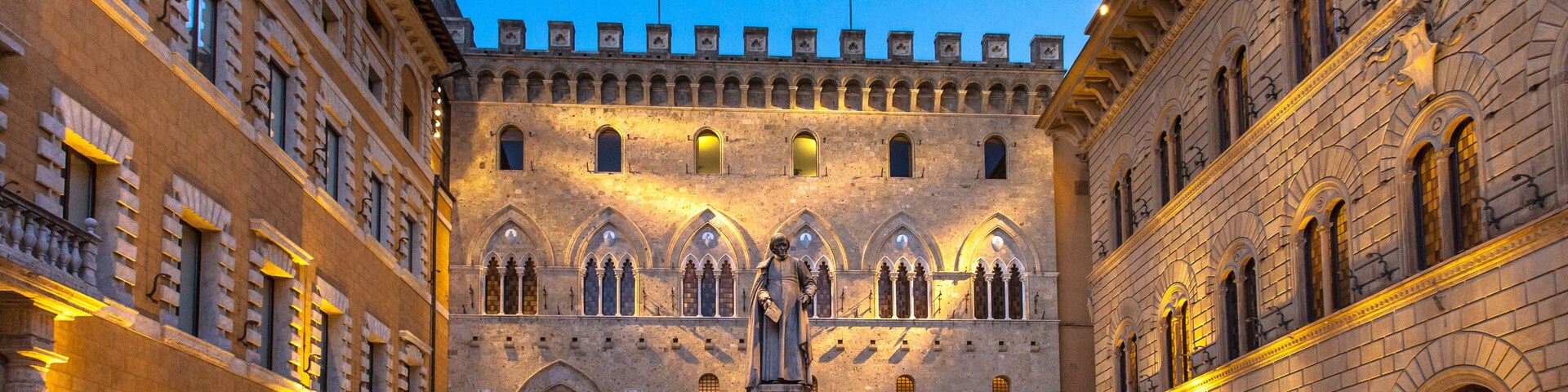 Um edifício histórico com janelas em arco e uma estátua em frente.